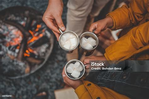 모닥불 근처에서 핫초코와 마시멜로가 든 금속 머그잔을 들고 있는 손을 클로즈업 따뜻하게 옷을 입고 어른과 아이가 공유하는 아늑한 야외 시간 가을에 대한 스톡 사진 및 기타