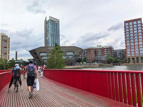 Pedestrians And A Cyclist Crossing The Striking Red Footbridge Of