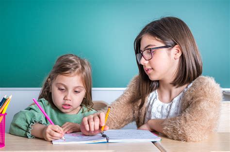 Older Sister Looks At Her Younger Sister As She Draws In A Notebook