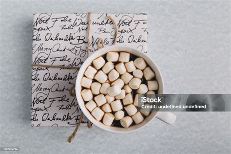 정사각형 선물은 밝은 파란색 질감의 배경에 놓여 있으며 위에는 핫 초콜릿이나 커피 마시멜로가 있는 흰색 머그잔이 있습니다 0명에 대한 스톡 사진 및 기타 이미지 Istock