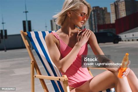 매력적인 젊은 여자 핑크 수영복 썬 안락에 앉아서 썬 스크린 로션 주차장에 적용 도시에 대한 스톡 사진 및 기타 이미지 도시 햇볕 차단 로션 건강한 생활방식 Istock