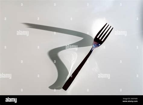 fork throws large elongate shadow on glass table background concept of