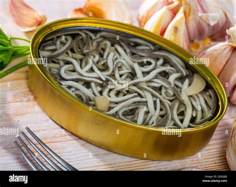 Open Tin Can Of Pickled Eels And Garlic With Greens At Table Stock