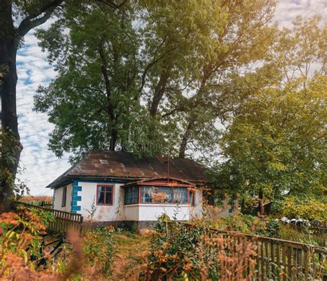 Neglected Abandoned House With An Old Fence Among Grass And Trees