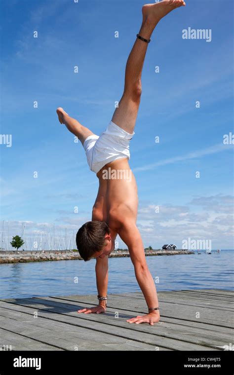 Male Teenager Doing An Acrobatic Handstand On A Jetty At The Beach One