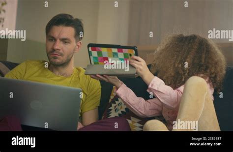 Young Dad Sitting On Sofa With Laptop An Eight Year Old Girl Shows Him Stock Video Footage Alamy
