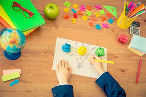 Criança Desenhando Lâmpada No Papel Itens Escolares Na Mesa De Madeira