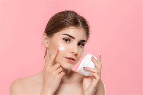 튜브에서 피부에 보습 크림을 적용 하는 아름 다운 여자 모델은 분홍색 배경 위에 격리 된 카메라를 봅니다 미용 및 건강 치료의