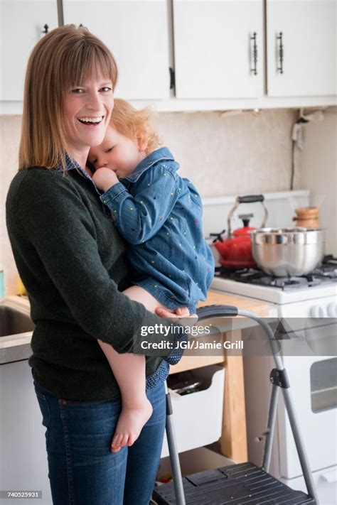 Caucasian Mother Holding Daughter Sucking Thumb In Kitchen High Res