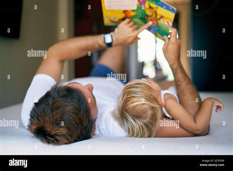 Dad Shows His Daughter A Book With Pictures Lying On The Bed Stock