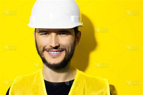 年轻的建筑师，建筑工程师的工作室肖像，穿着建筑安全头盔和反光夹克在黄色的背景。