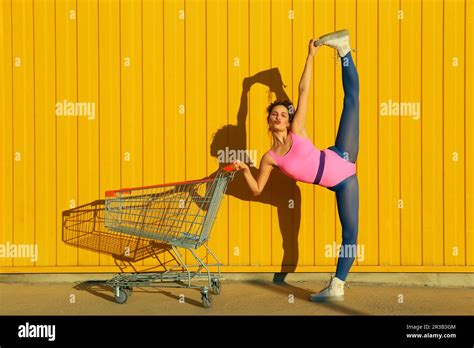 Ballet Dancer Doing Vertical Split By Shopping Cart In Front Of Yellow