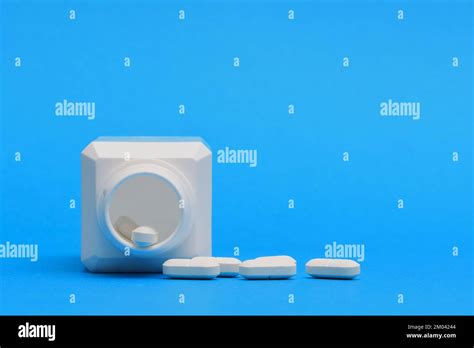 A White Open Prescription Medication Container With Some Tablets Out On A Blue Cardboard