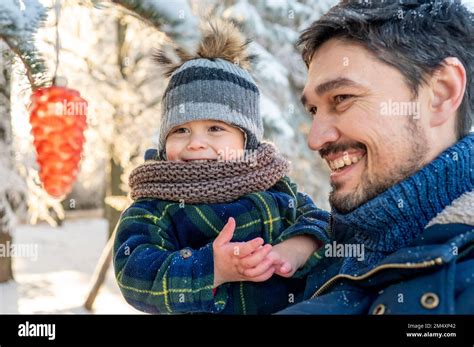 Happy Man With Son Looking At Pine Cone Hanging On Branch Of Christmas