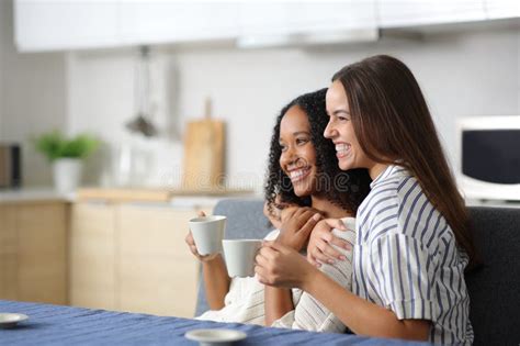 Happy Interracial Lesbian Couple Hugging In The Kitchen Looking Away Stock Image Image Of