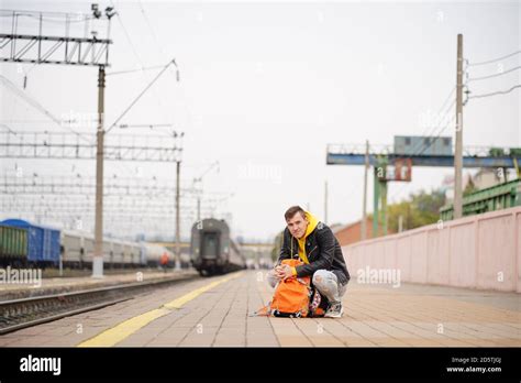 Young Man Squats On Platform Waiting For Train Male Passenger With