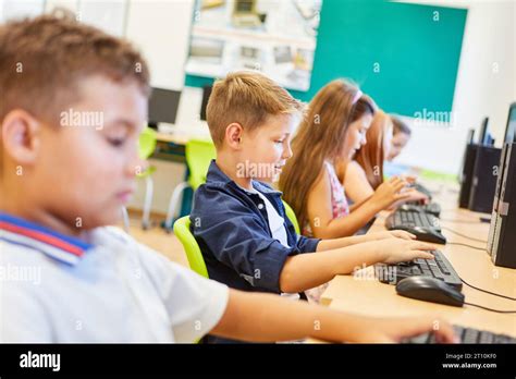 Elementary Schoolboy Typing On Keyboard While Sitting With Friends In