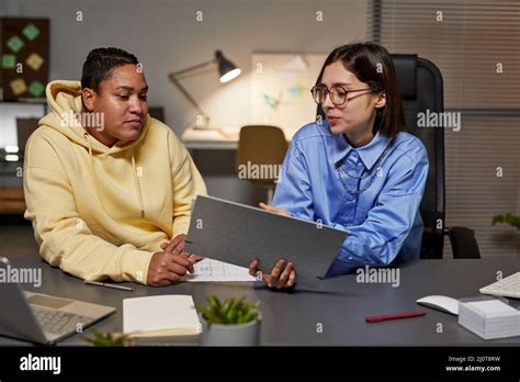 Portrait Of Two Young Women Discussing Documentation While Working Late