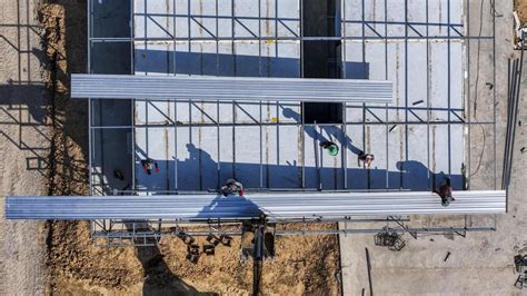 Aerial View Of Workers Placing Long Metal Sheets Onto A Building