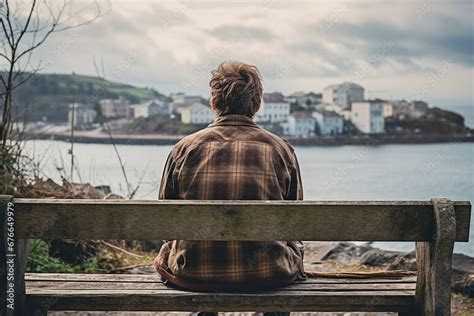 Un Hombre Joven Sentado En Un Banco En La Orilla Del Mar Al Fondo Se Ve Un Pequeño Pueblo Con