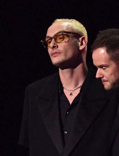 Two Men Standing Next To Each Other In Front Of A Dark Background With One Man Wearing Sunglasses