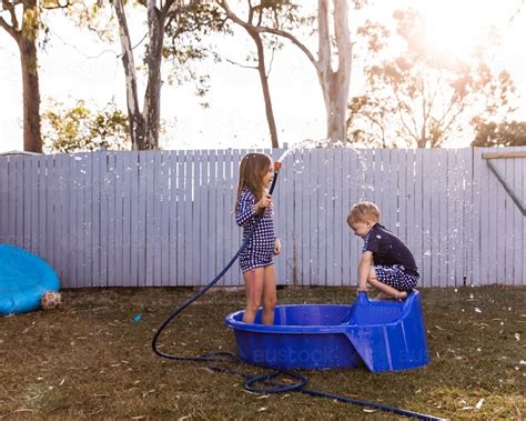 Image Of Brother And Sister Playing With The Hose In The Back Yard