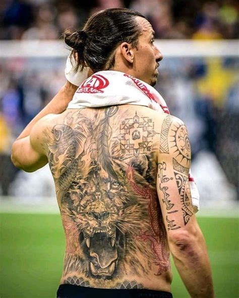 A Man With Tattoos On His Back Standing In Front Of A Soccer Field And