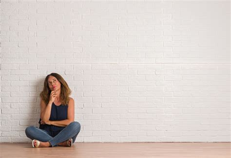 중세 스페인 여자 손으로 턱 질문 잠겨있는 표현에 대 한 생각에 흰색 벽돌 벽을 통해 바닥에 앉아 사려깊은 얼굴 미소 의심 개념입니다 갈색 머리에 대한 스톡 사진 및 기타