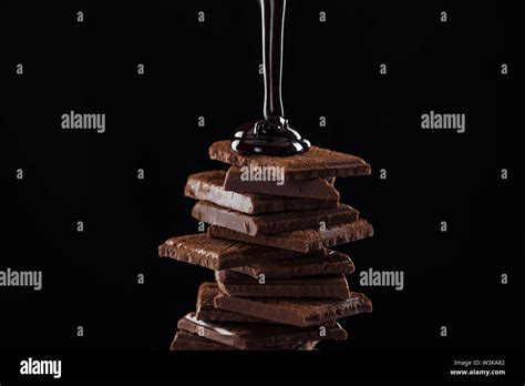 Hot Melted Dark Chocolate Pouring On Chocolate Stack Isolated On Black