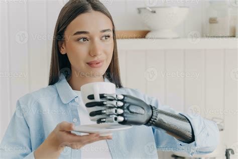 A Young Woman With A Bionic Prosthetic Hand Admiringly Holds A Cup A