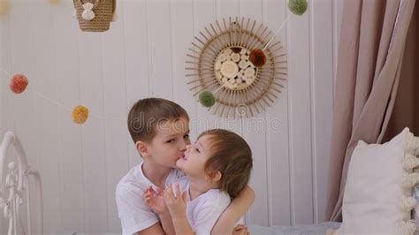 Brother And Sister Cuddle Sitting At Home On The Bed In The Bright