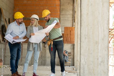 A Female Architect And Construction Managers Work Together On Site Discussing Blueprints And
