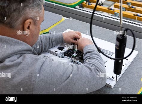 Photo Of An Adult Man In A Gray Sweater Who Assembles A Computer Monitor System Block On An