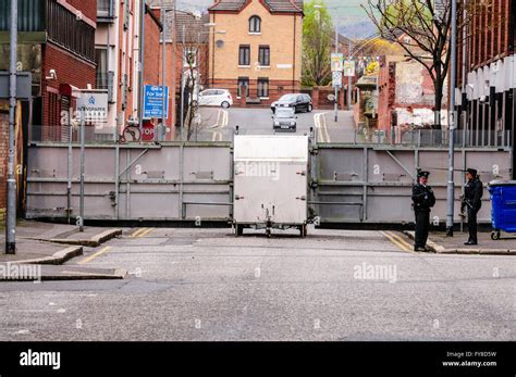 Two Psni Officers Stand By A Large Metal Mobile Police Cordon Barrier