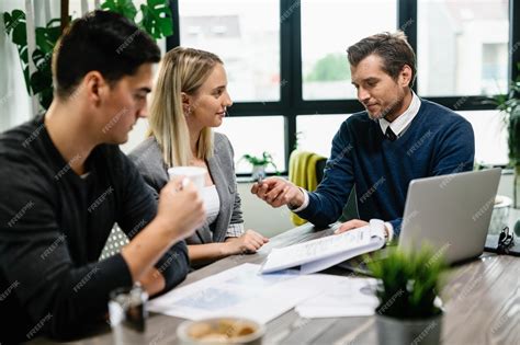 Happy Real Estate Agent Showing To Young Couple A Mortgage Contract On