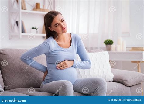 Pregnant Lady Having Backache Massaging Back Sitting On Sofa Indoor