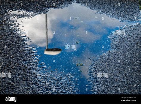 Water Puddle On Textured Asphalt Reflection Of Streetlamp Sky Clouds