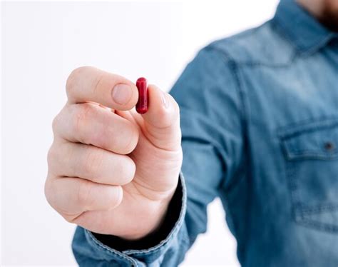 Premium Photo Man Holding A Small Red Capsule Pill Closeup