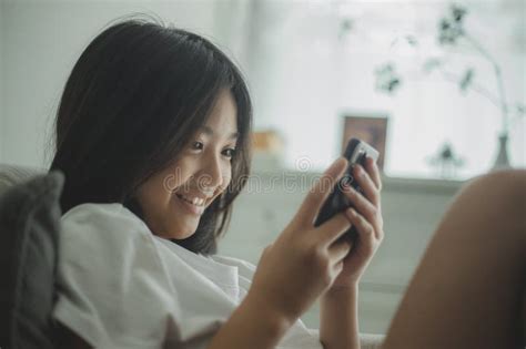 Happy Asian Girl Relaxing On A Comfortable Couch At Home Texting And