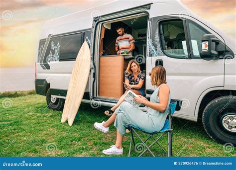 Two Women Talking In Front Of Camper Van While Young Man Cooks Stock