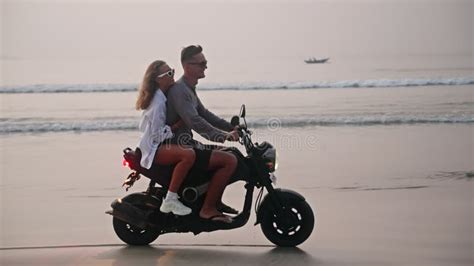 Romantic Couple Ride Motorbike On Ocean Beach On A Date At Sunrise