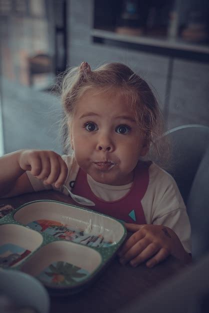 Premium Photo Portrait Of A Girl Sitting On Table And Eats