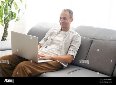 Young Male Tech User Relaxing On Sofa Holding Laptop Computer Mock Up
