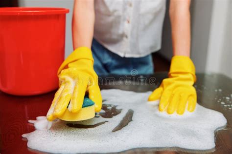 Woman In Rubber Gloves Cleaning Table With Sponge And Bucket Of Soapy Water In Front Of Red