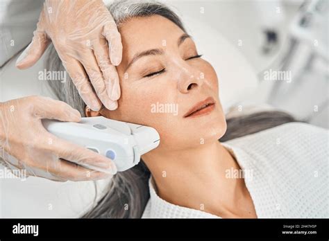 Pleased Asian Patient Enjoying The Procedure Of Smoothing Skin Stock