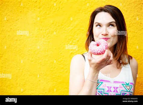 Young Brunette Woman Eating A Donut In Front Of Yellow Background Stock