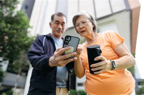 Elderly Asian Man And Woman Connecting Mobile Phone To A Smart Speaker