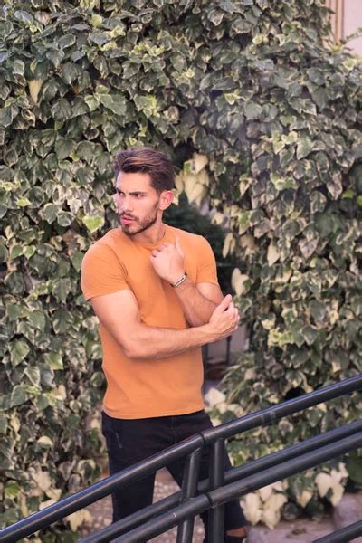 Metrosexual Male With Fit Body In Orange T Shirt And Jeans Standing On Staircase Against Tree In