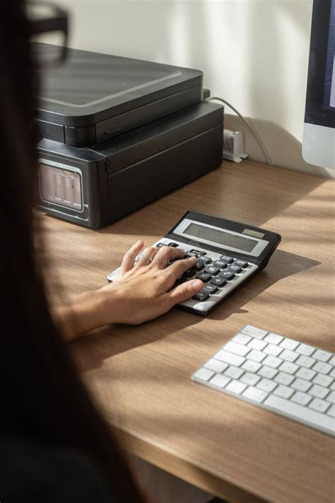A Woman With Long Hair Uses A Calculator In A Workspace With A Printer