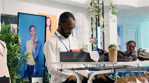 Retail Assistant Working In Luxury Fashion Boutique Placing Clothes On